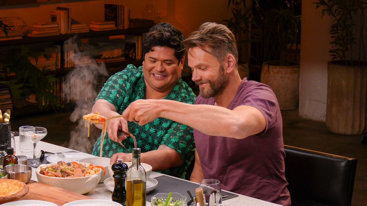 Harvey Guillén and Joel McHale serving food to each other.